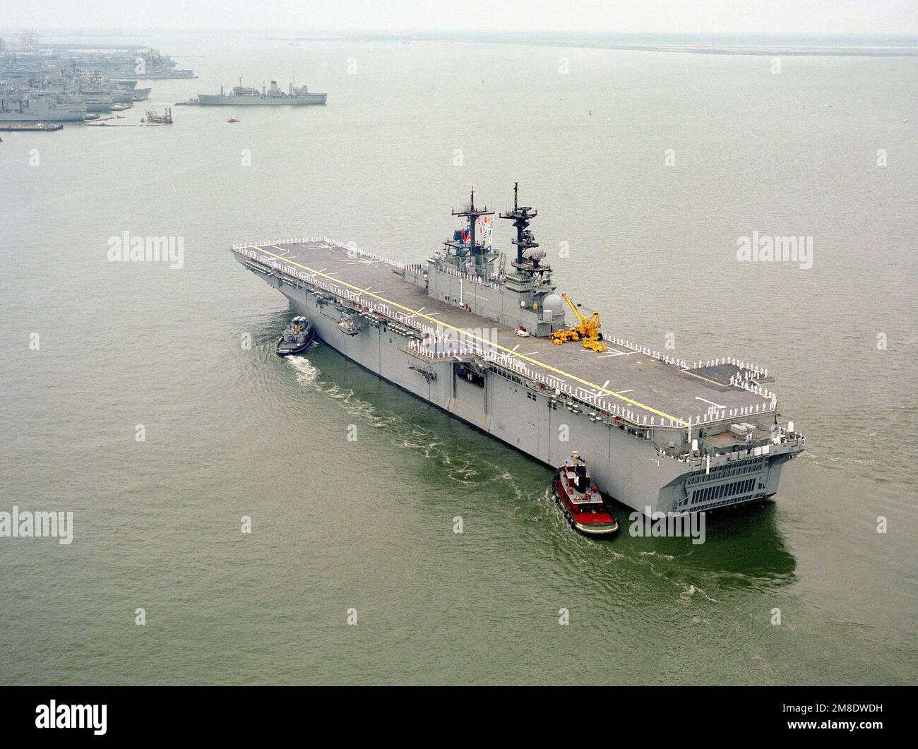 Crew members man the rails as harbor tugs maneuver the amphibious ...