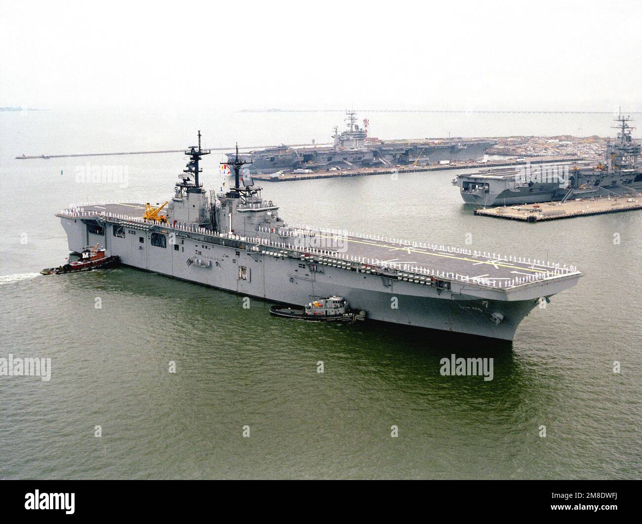 Crew members man the rails as harbor tugs maneuver the amphibious ...