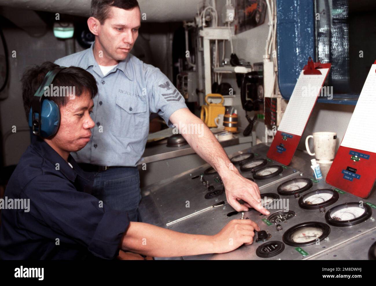 A first class petty officer points out a gauge to a sailor monitoring a ...