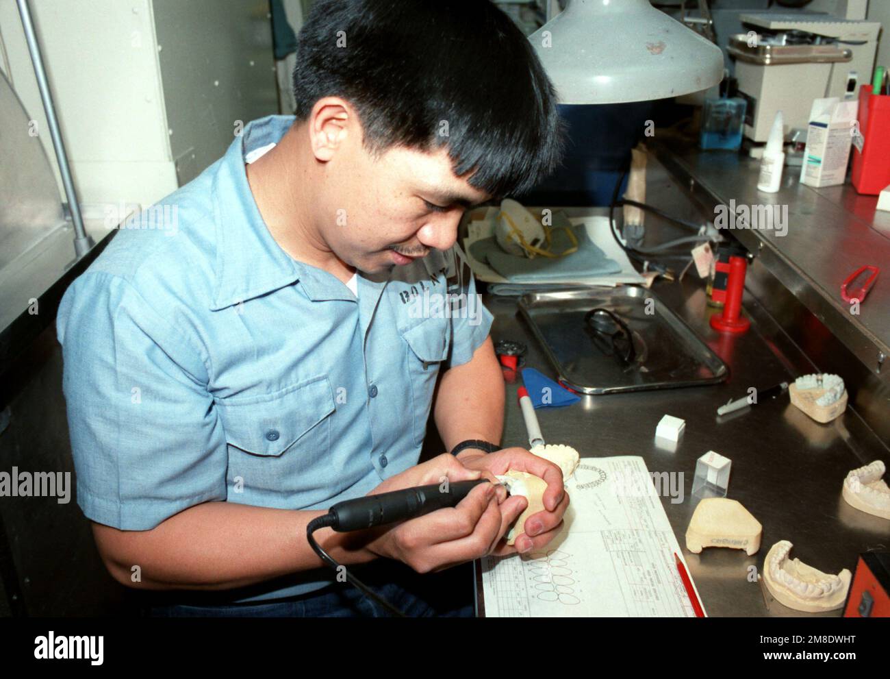 A petty officer polishes the teeth on a set of dentures he is making ...