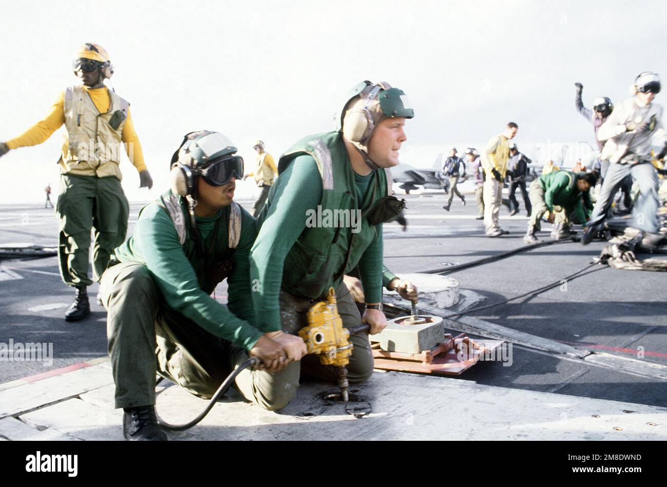 Flight deck crew members use a pneumatic wrench to release the safety ...