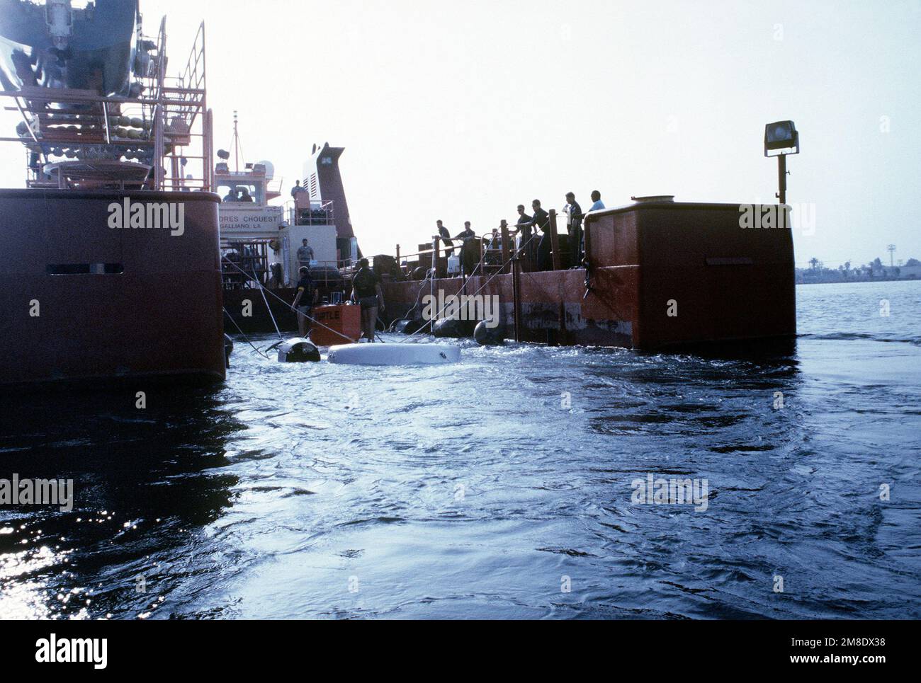 Crew members aboard the civilian support ship DOLORES CHOUEST hold onto ...