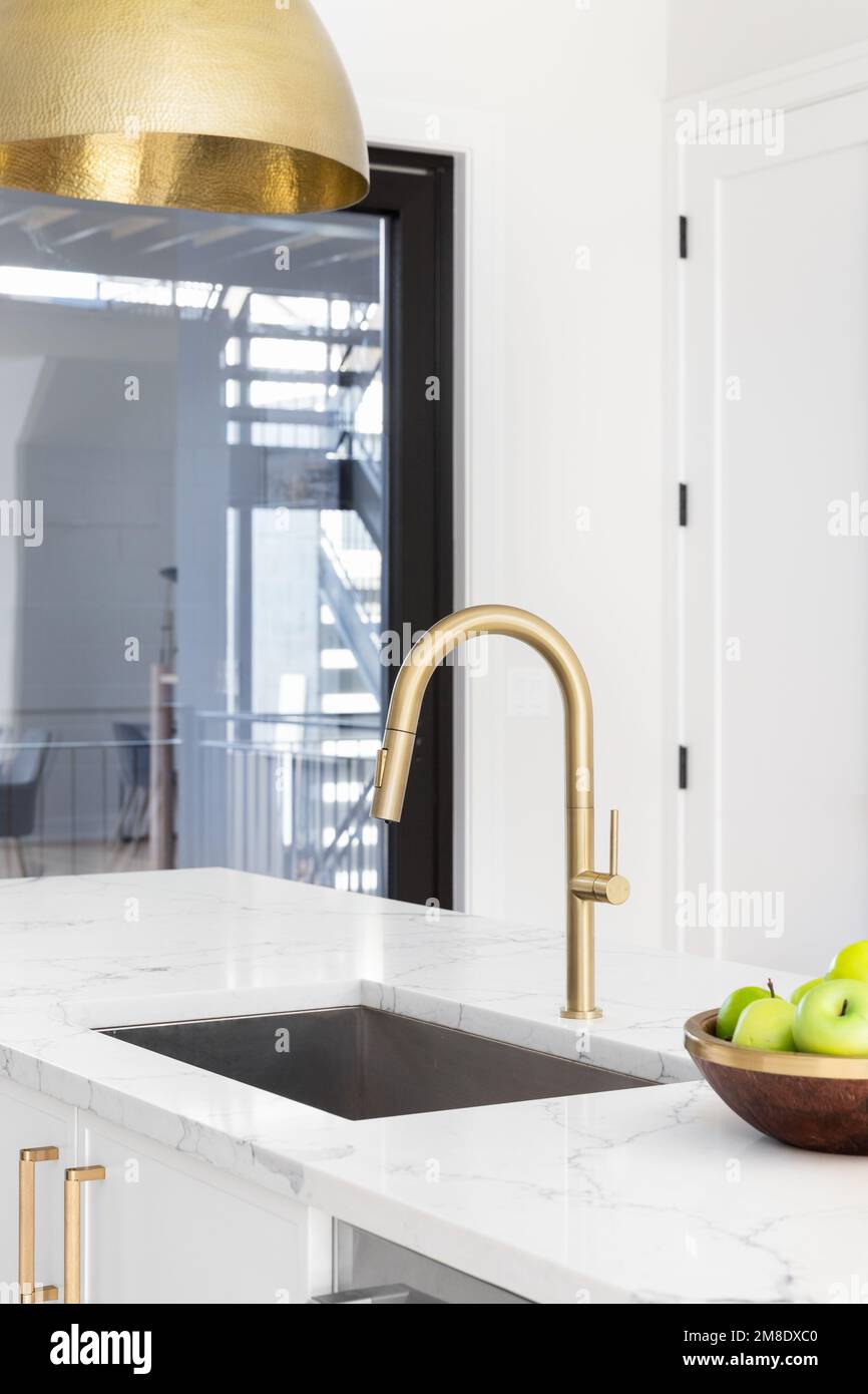 A gold kitchen faucet in a white kitchen with a marble countertop, gold ...
