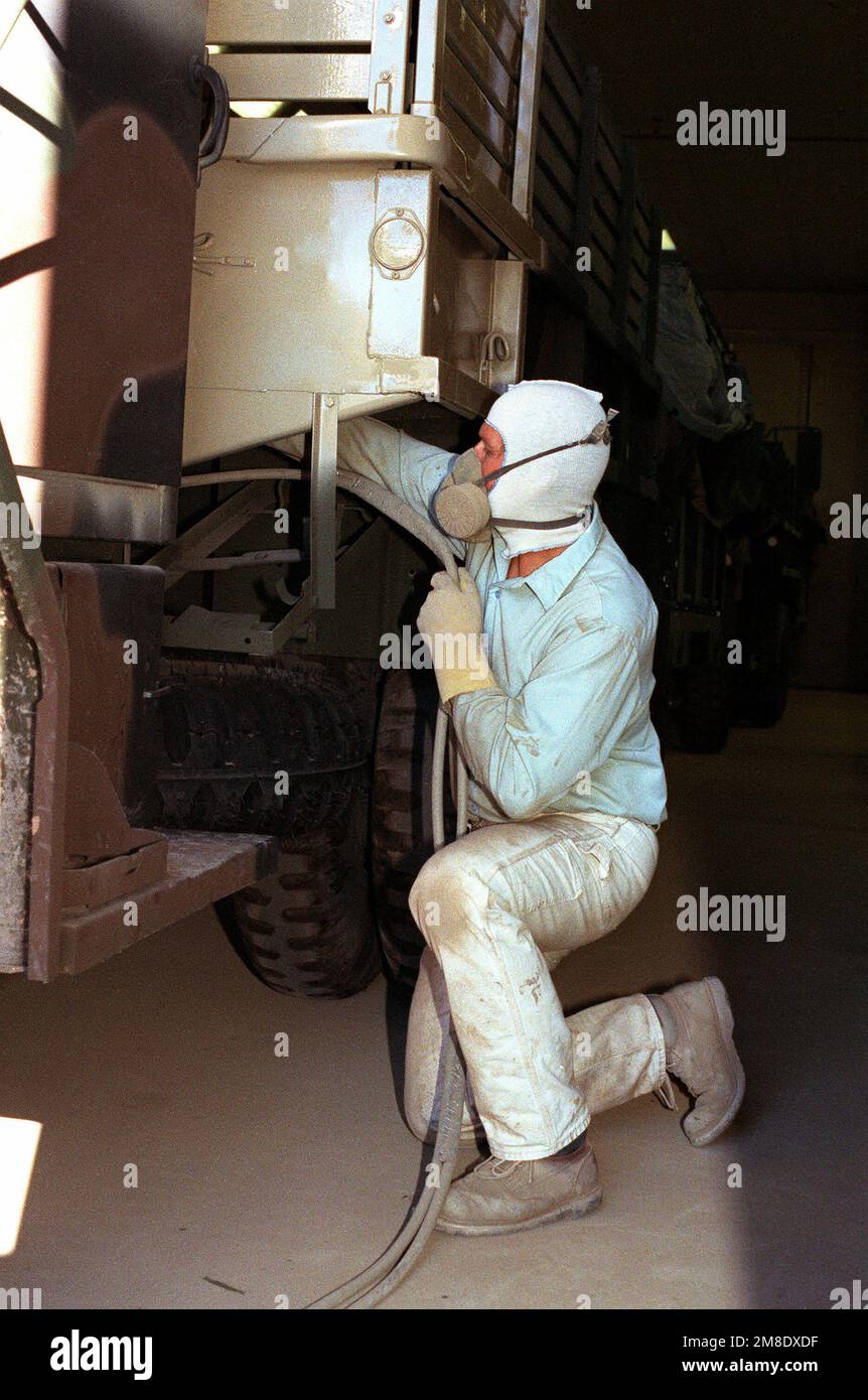 A civilian contractor uses a spray gun to apply a coat of desert ...
