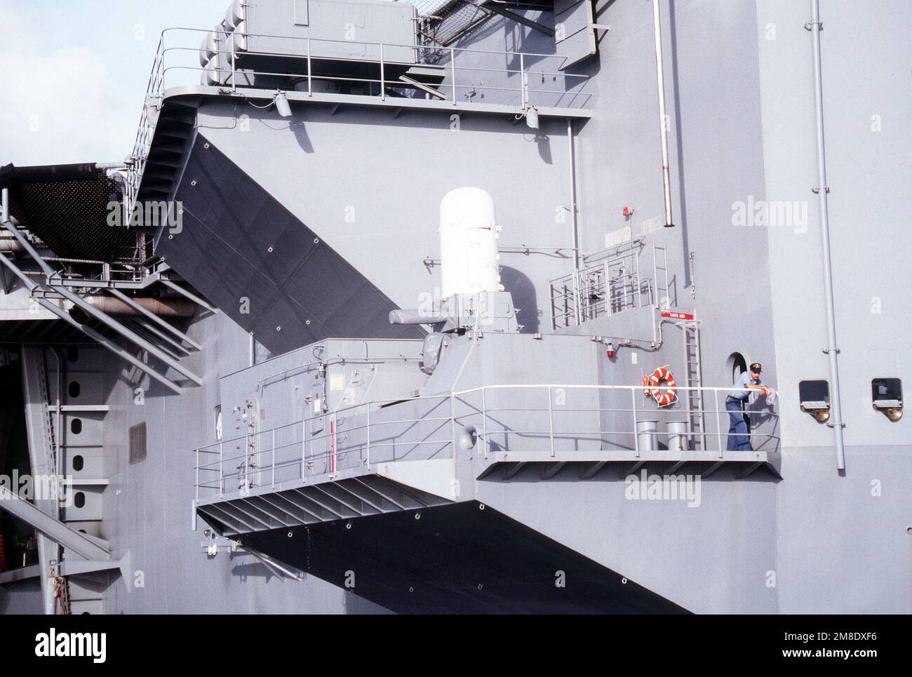 A sailor leans on a railing near the Mark 16 Phalanx close-in weapon ...