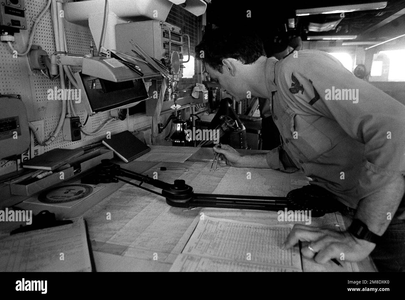 A crew member plots a bearing on a chart on the bridge of the guided ...