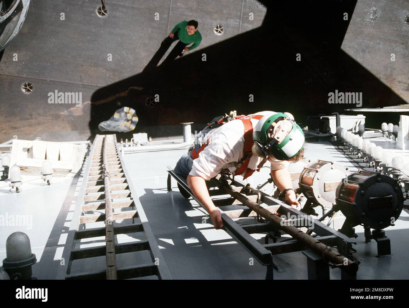 A sailor wearing a helmet and safety harness climbs a ladder to change ...