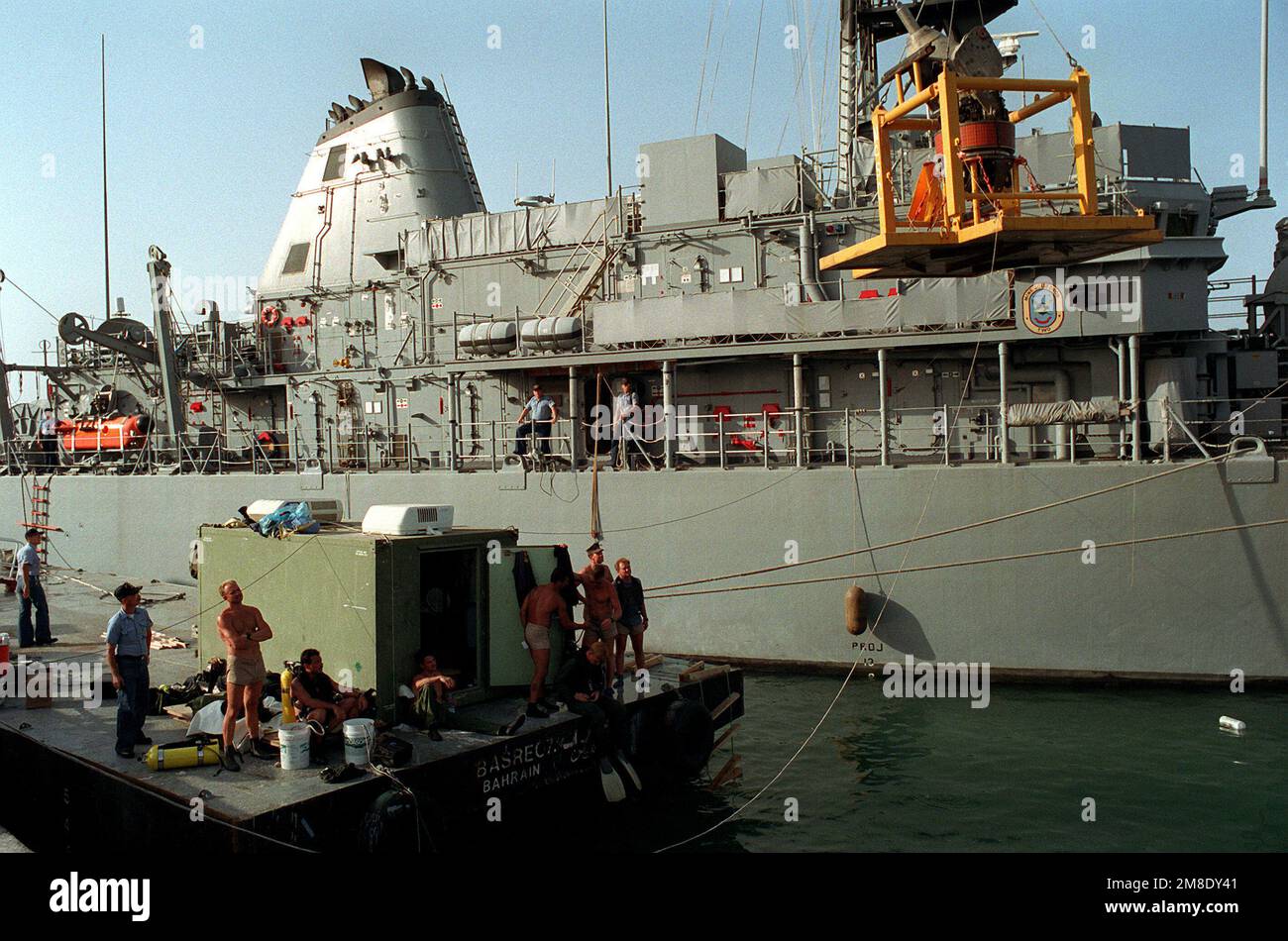 Divers watch from a barge as a component of the mine countermeasures ...