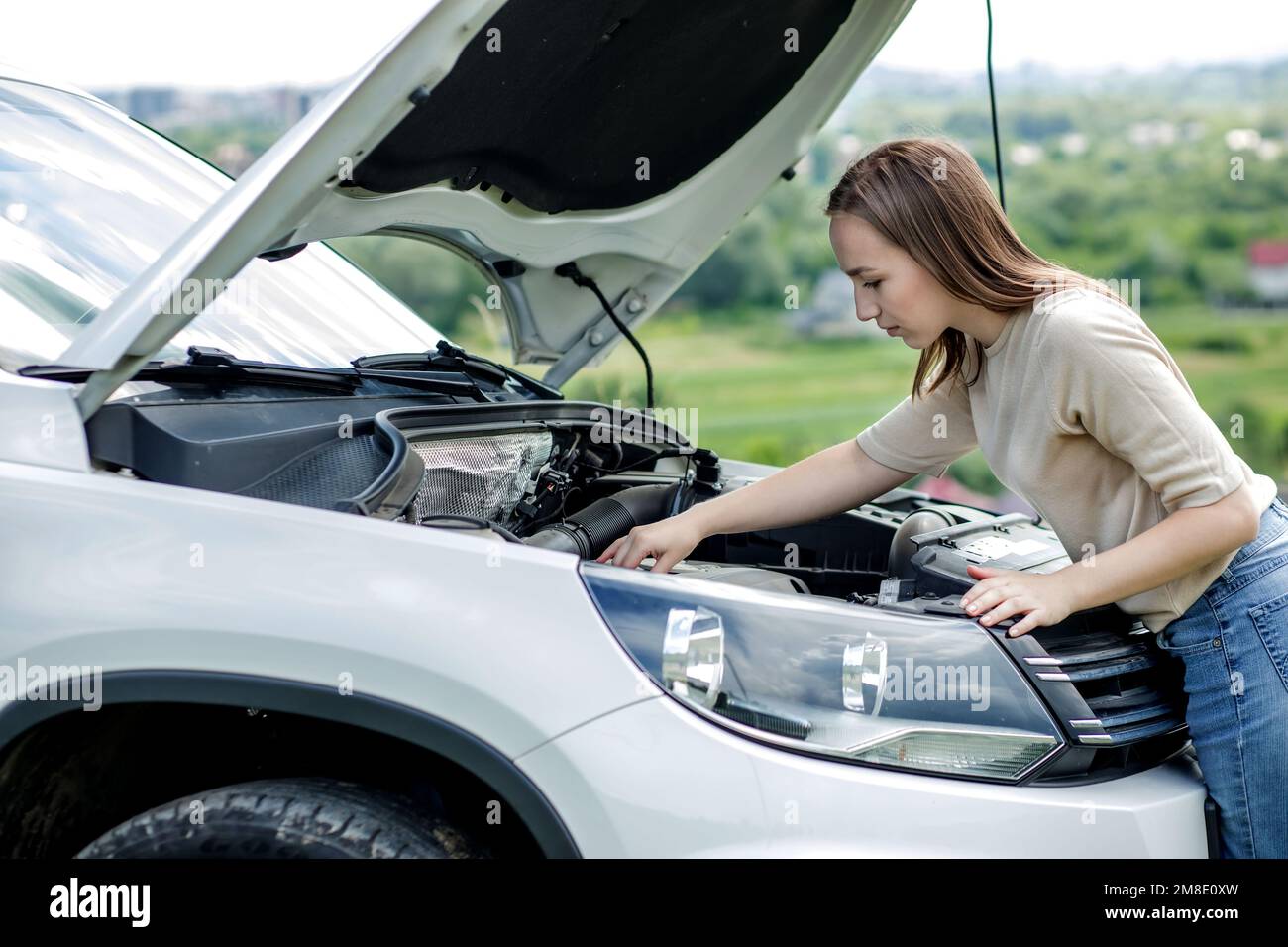 Confused female driver standing outside her car with the hood up ...
