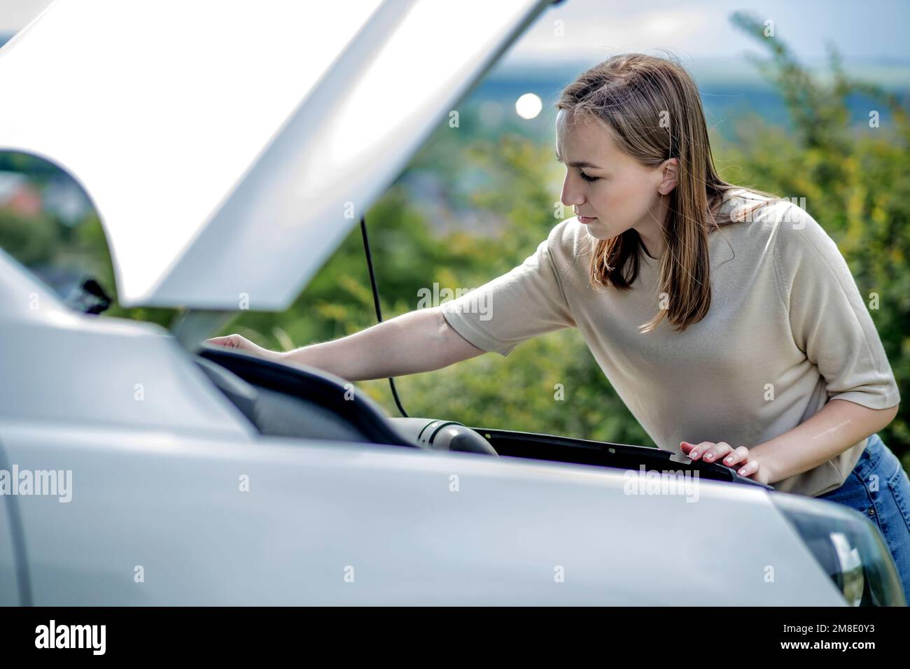 Confused female driver standing outside her car with the hood up ...