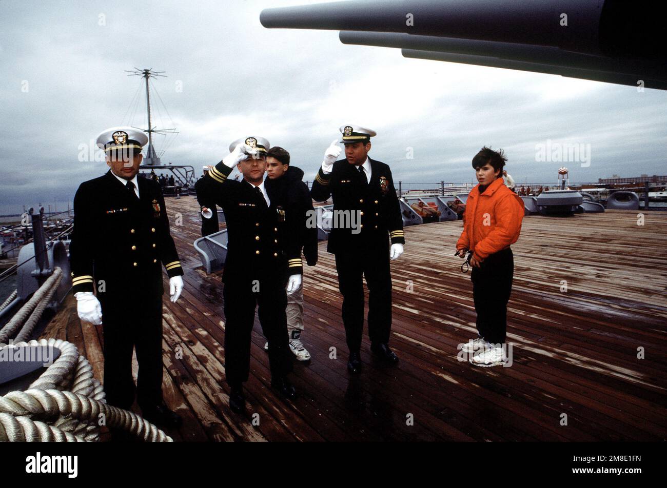 Three officers and their guests stand on the deck of the battleship USS ...