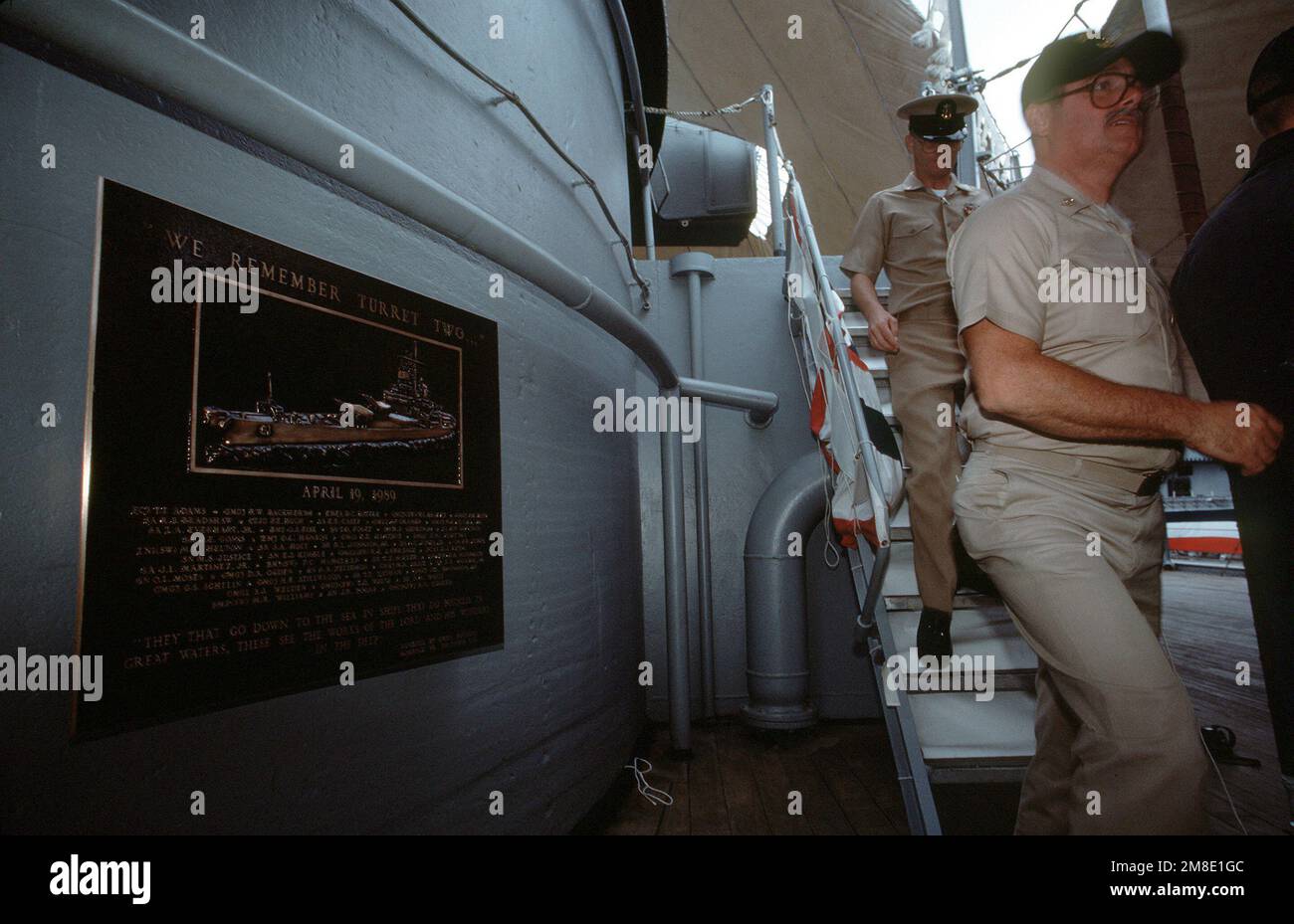 Two chief petty officers walk past a plaque aboard the battleship USS ...