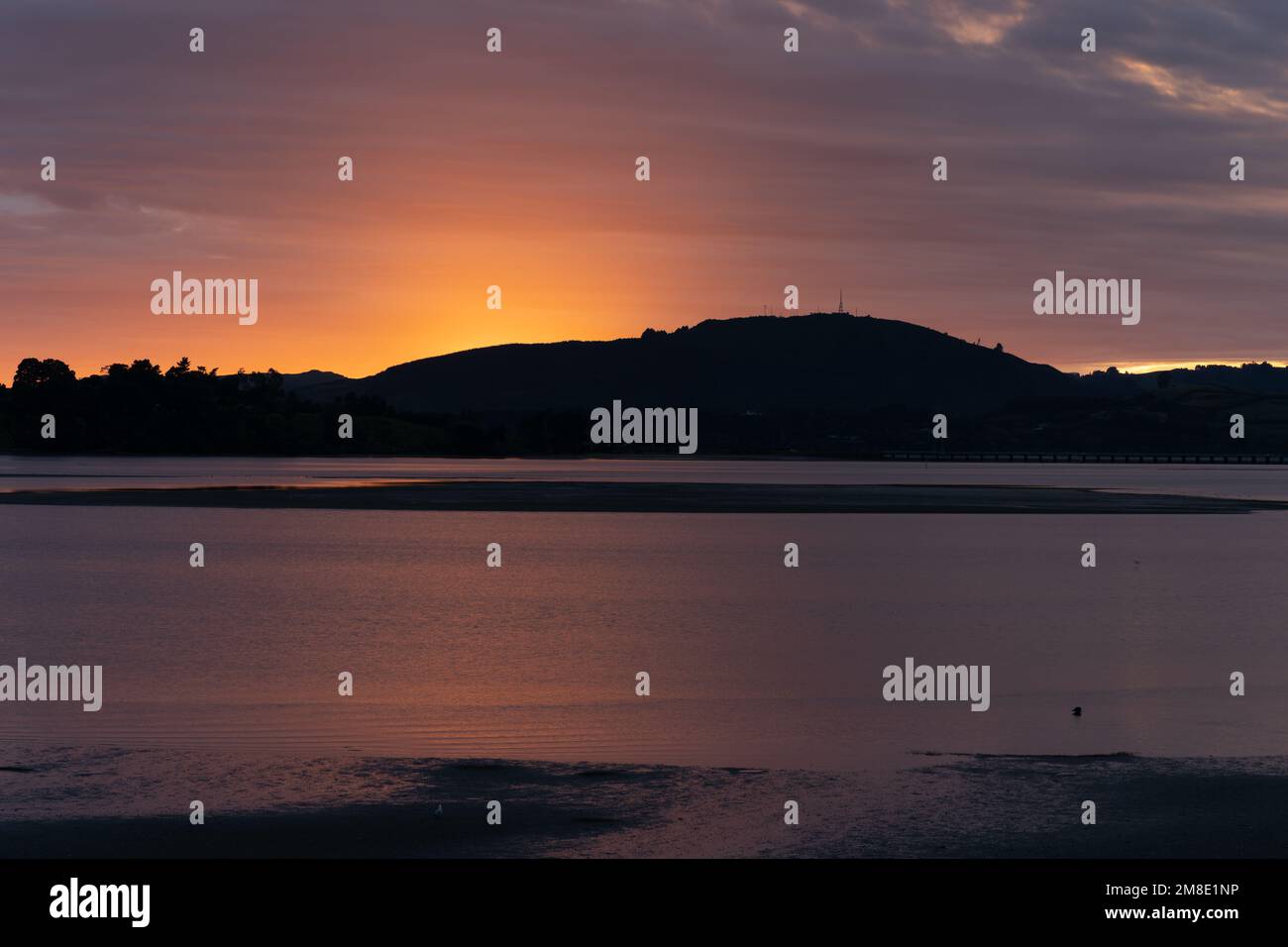 Bright orange sunset glow of over land in silhouette and below clouds ...