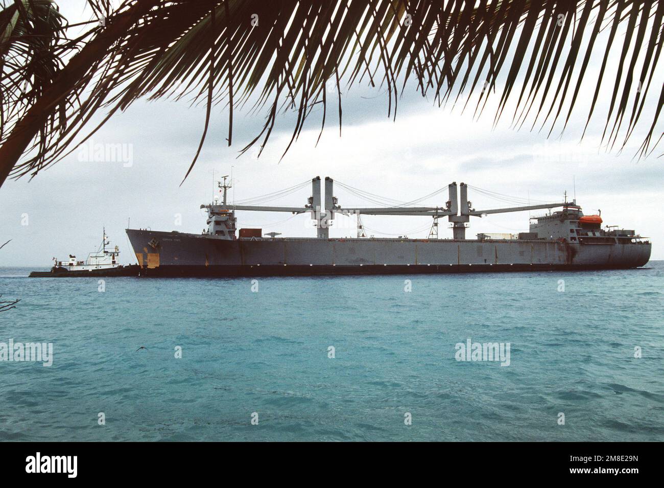 A tug boat assists the Military Sealift Command auxiliary crane ship ...