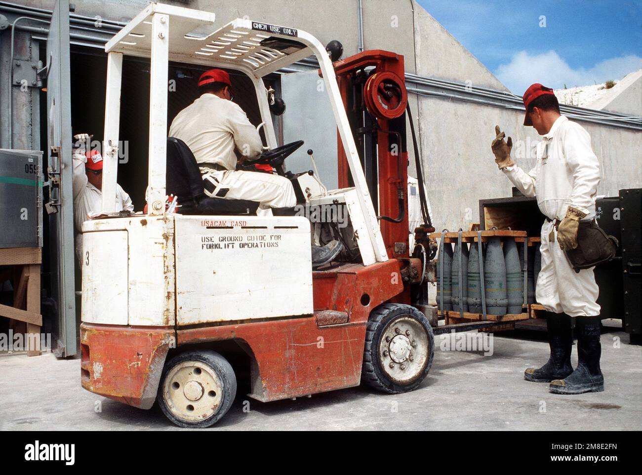 A soldier directs the driver of a forklift as he removes a pallet of ...