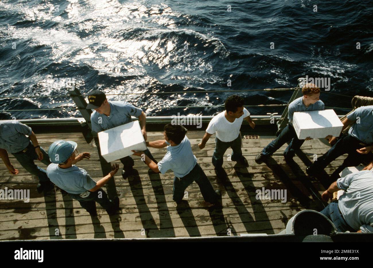 Sailors pass along boxes while on a working party aboard the battleship ...