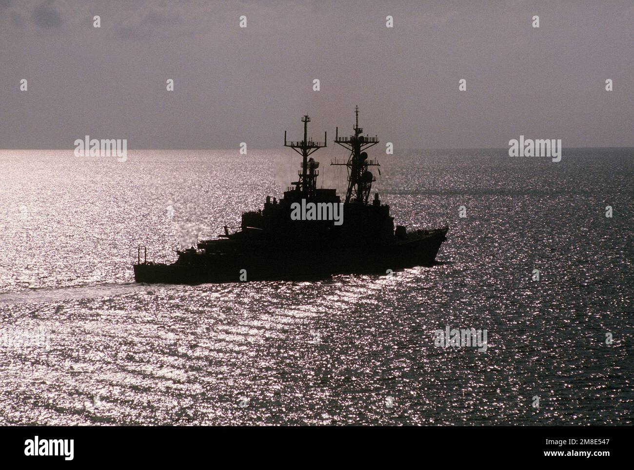 The destroyer USS SPRUANCE (DD-963) is silhouetted by the sun while ...