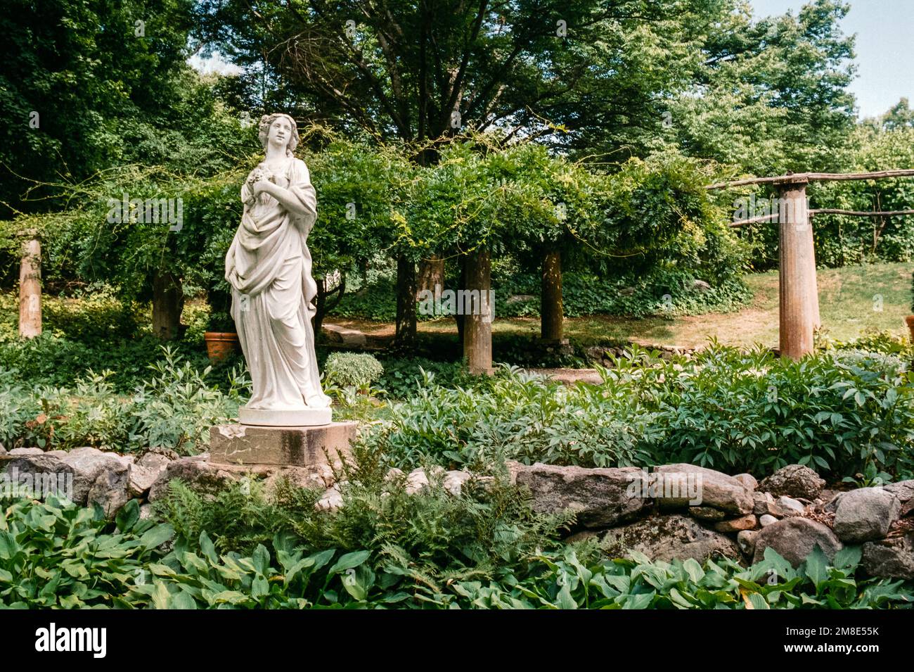 A white statue of a goddess stands in front of a stone grape trellis in ...