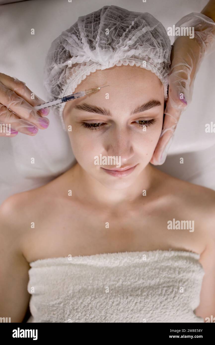 A young woman receives an injection of anti-aging botox filler in the ...