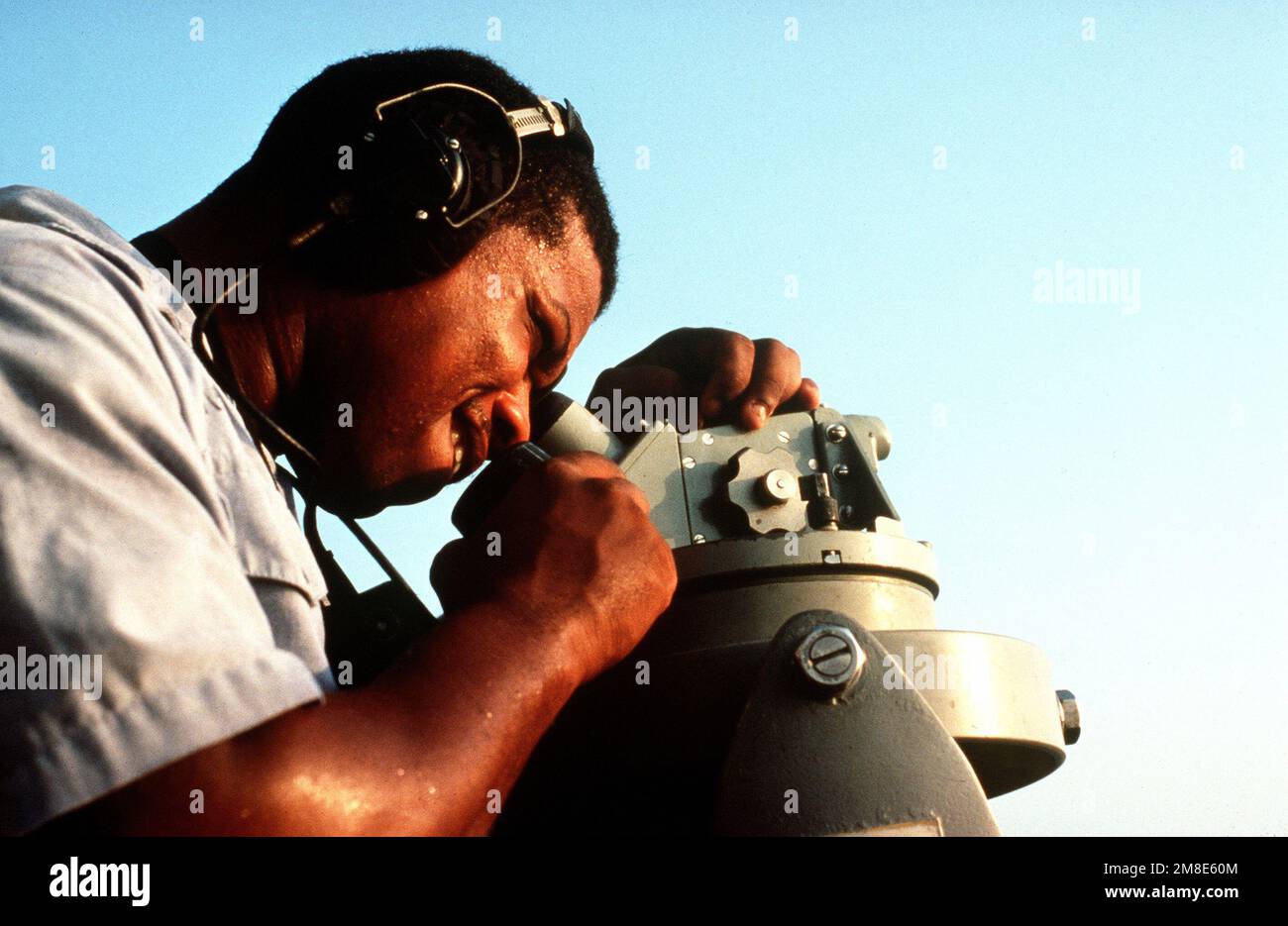 A crewman aboard a minesweeper takes a bearing with a telescopic ...