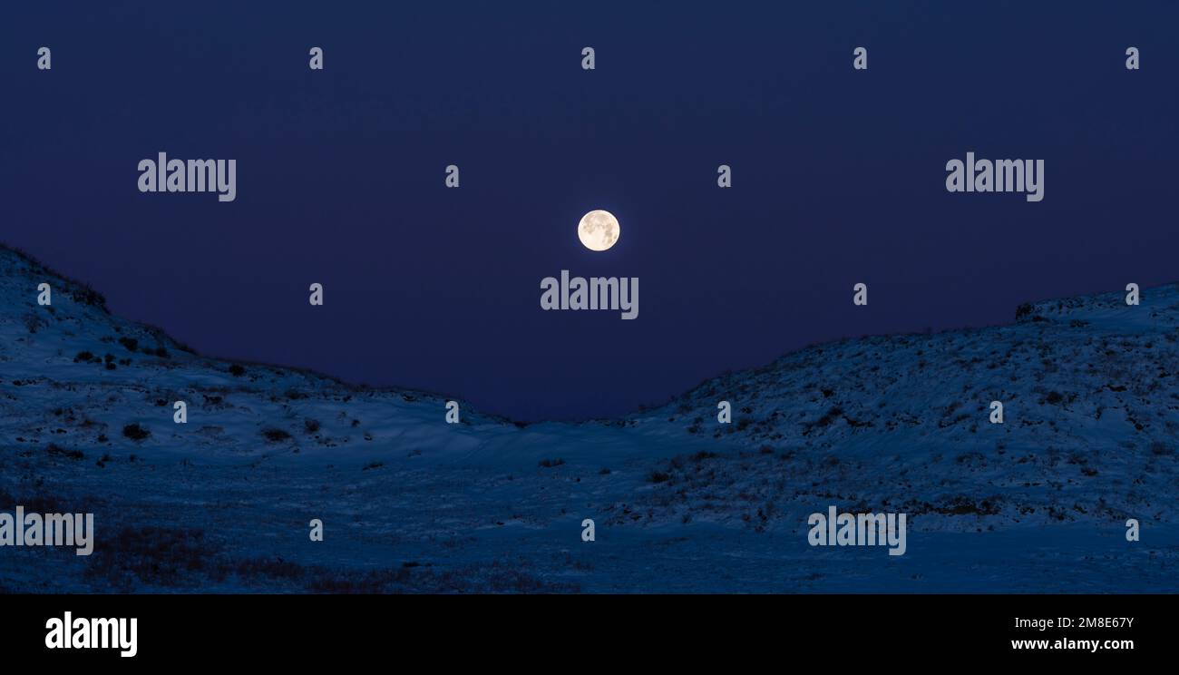 A full moon setting at dawn over a snowy landscape at Theodore ...
