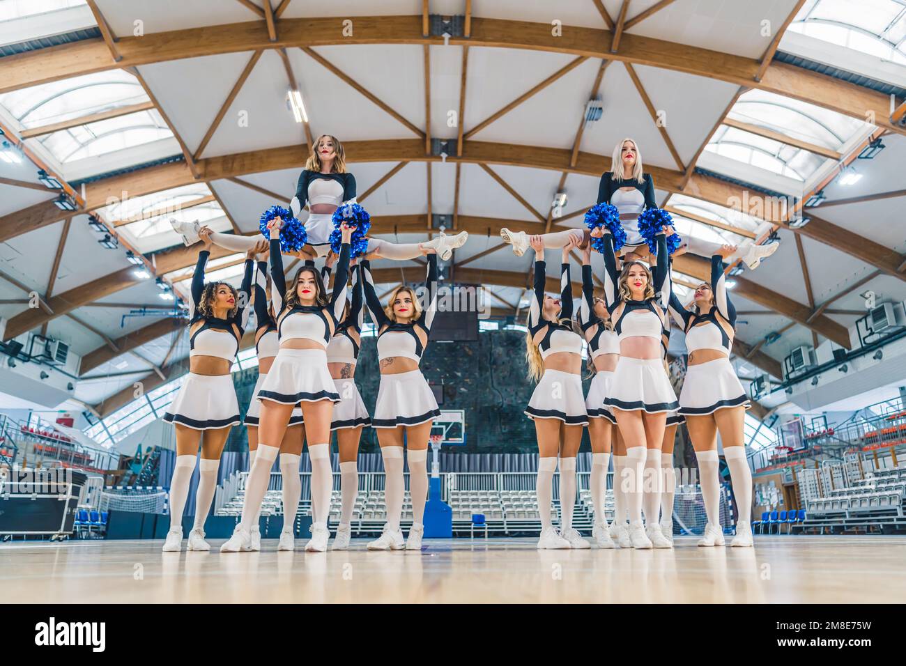 Cheerleaders with vibrant pom-poms executing a split lift stunt on an indoor court Stock Photo ...