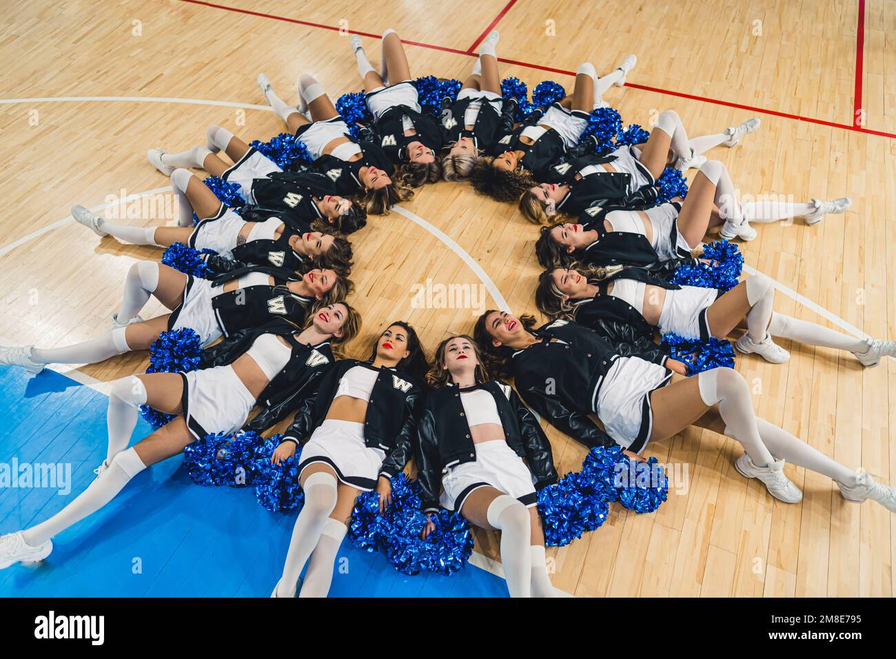 A group of cheerleaders lying on the floor forming a circle with their ...