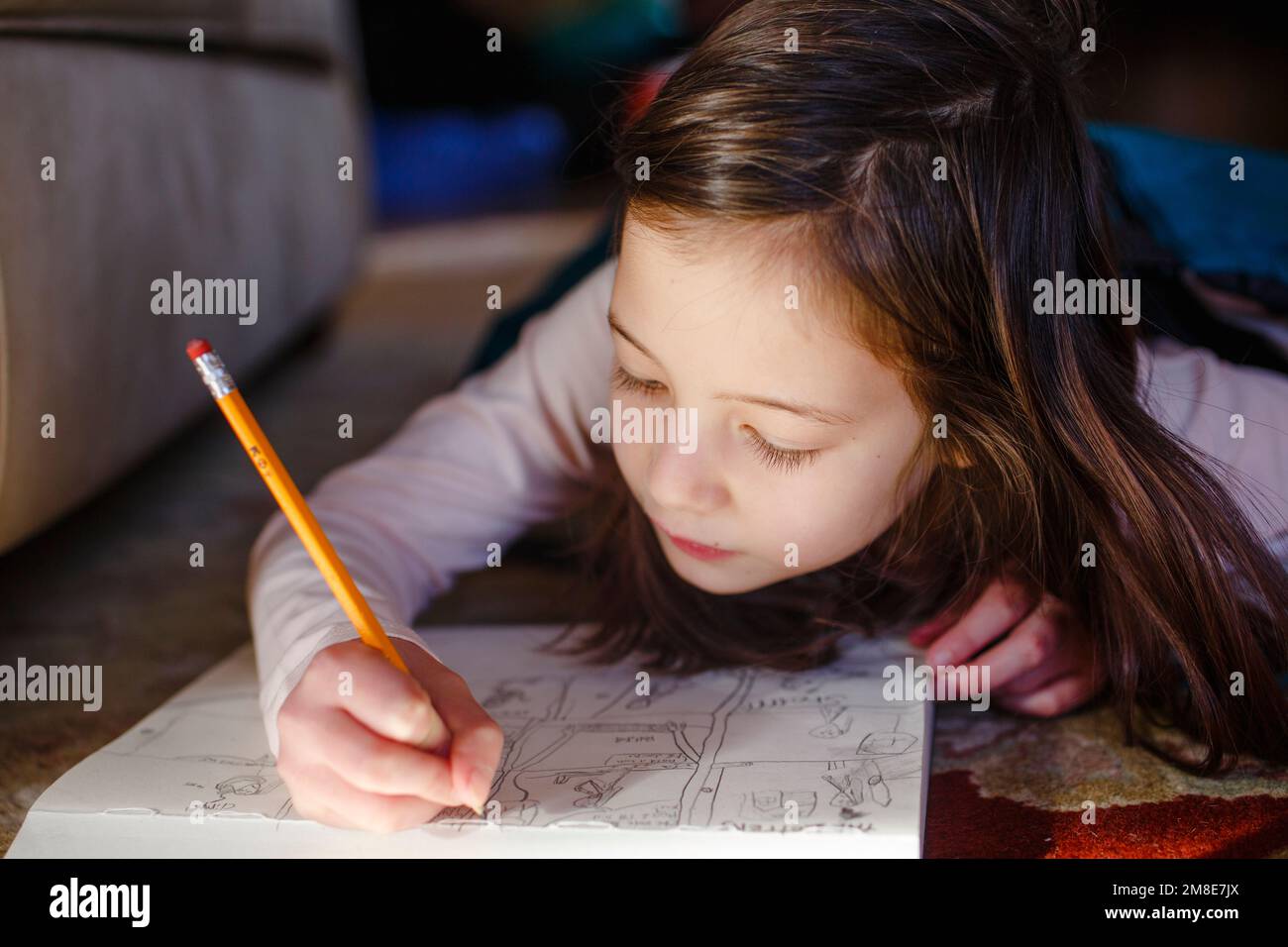 A little girl lays on floor carefully drawing in a sketchpad Stock ...