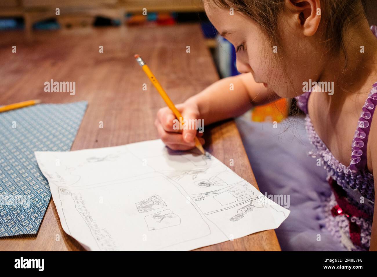 A little girl sis at table in costume carefully drawing a comic Stock ...