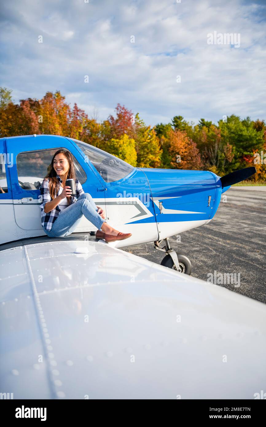 Young BIPOC Female Pilot having morning coffee on small plane wing ...