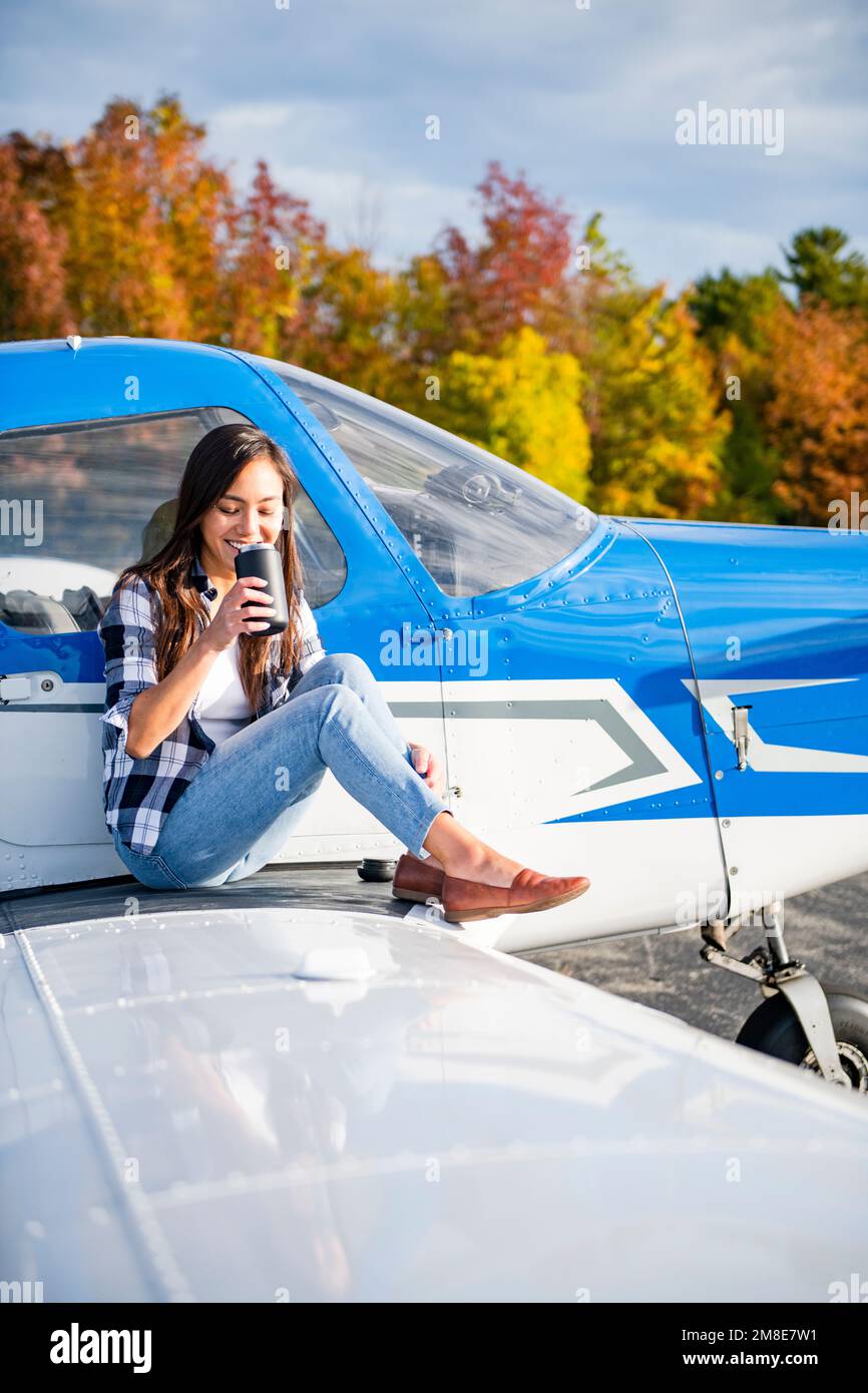 Young BIPOC Female Pilot sipping morning coffee on small plane wing ...