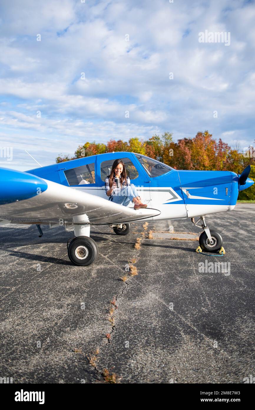 Young BIPOC Female Pilot having morning coffee on small plane wing ...
