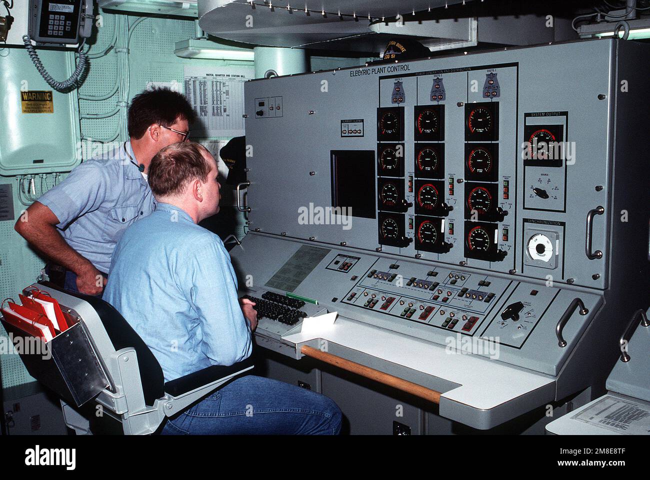 Two sailors work at the electric plant control console in an ...