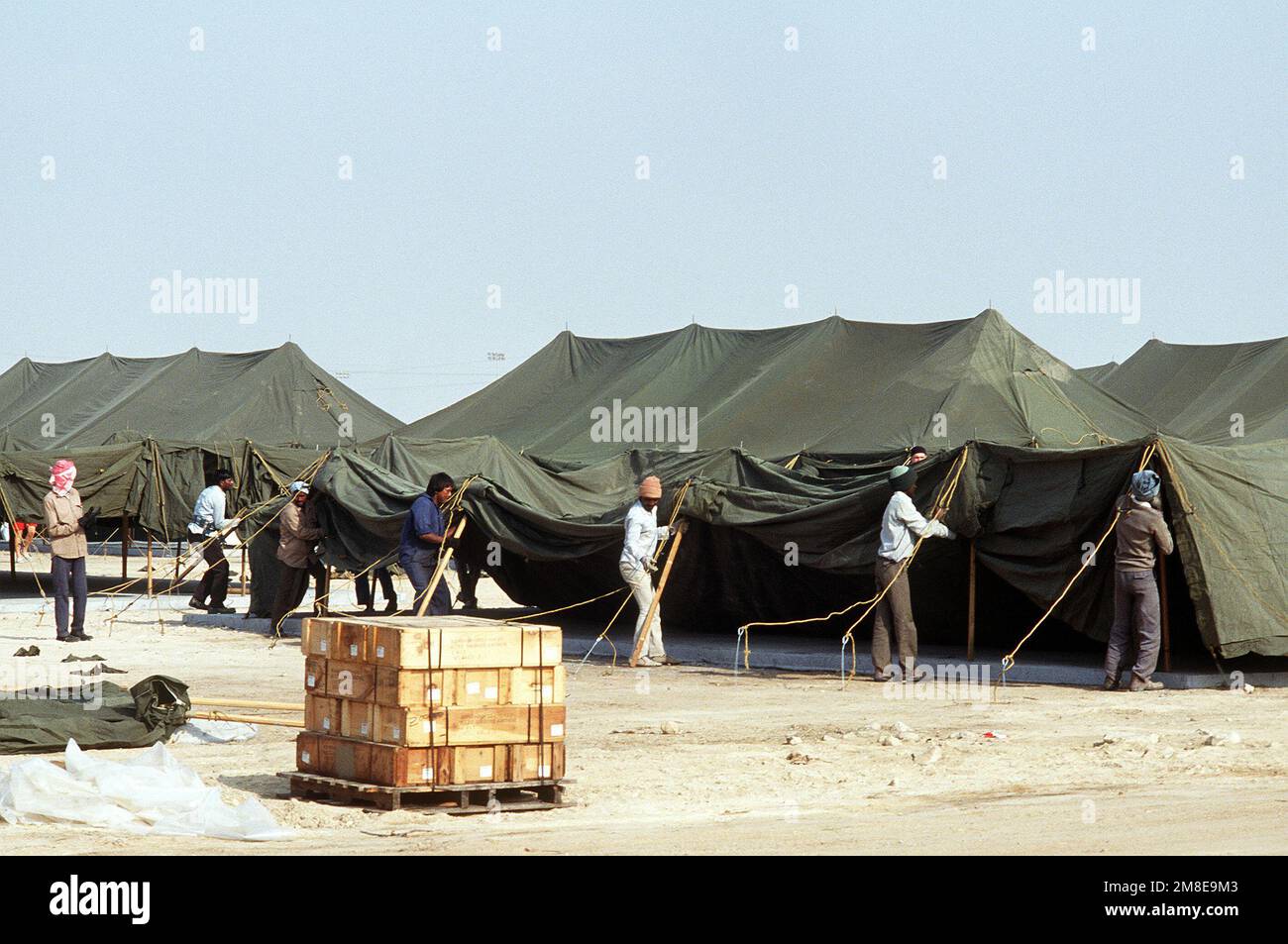 Civilian contract workers raise one side of a tent as they assist in ...