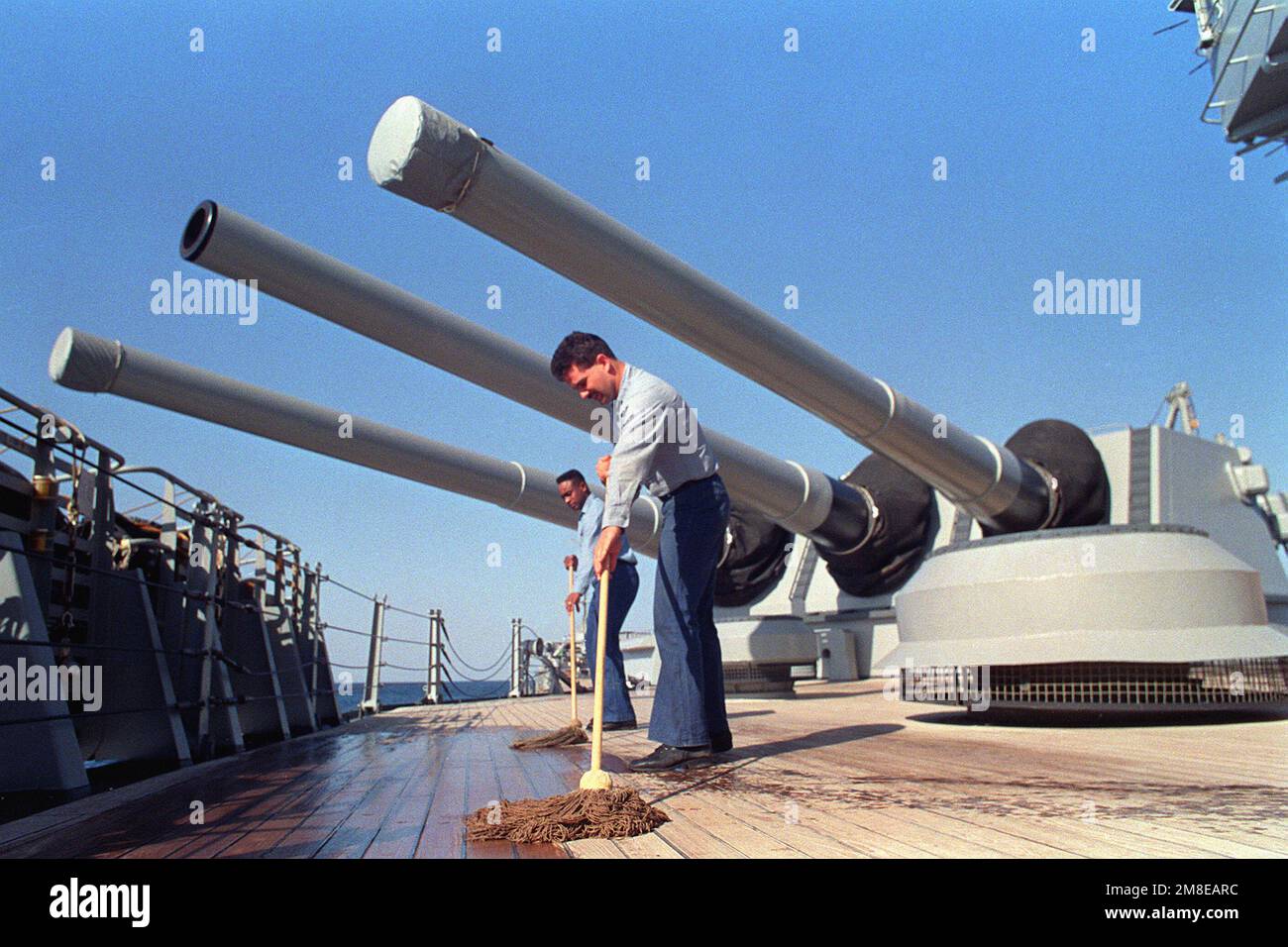 Sailors swab the wooden deck near the No. 2 gun turret aboard the ...