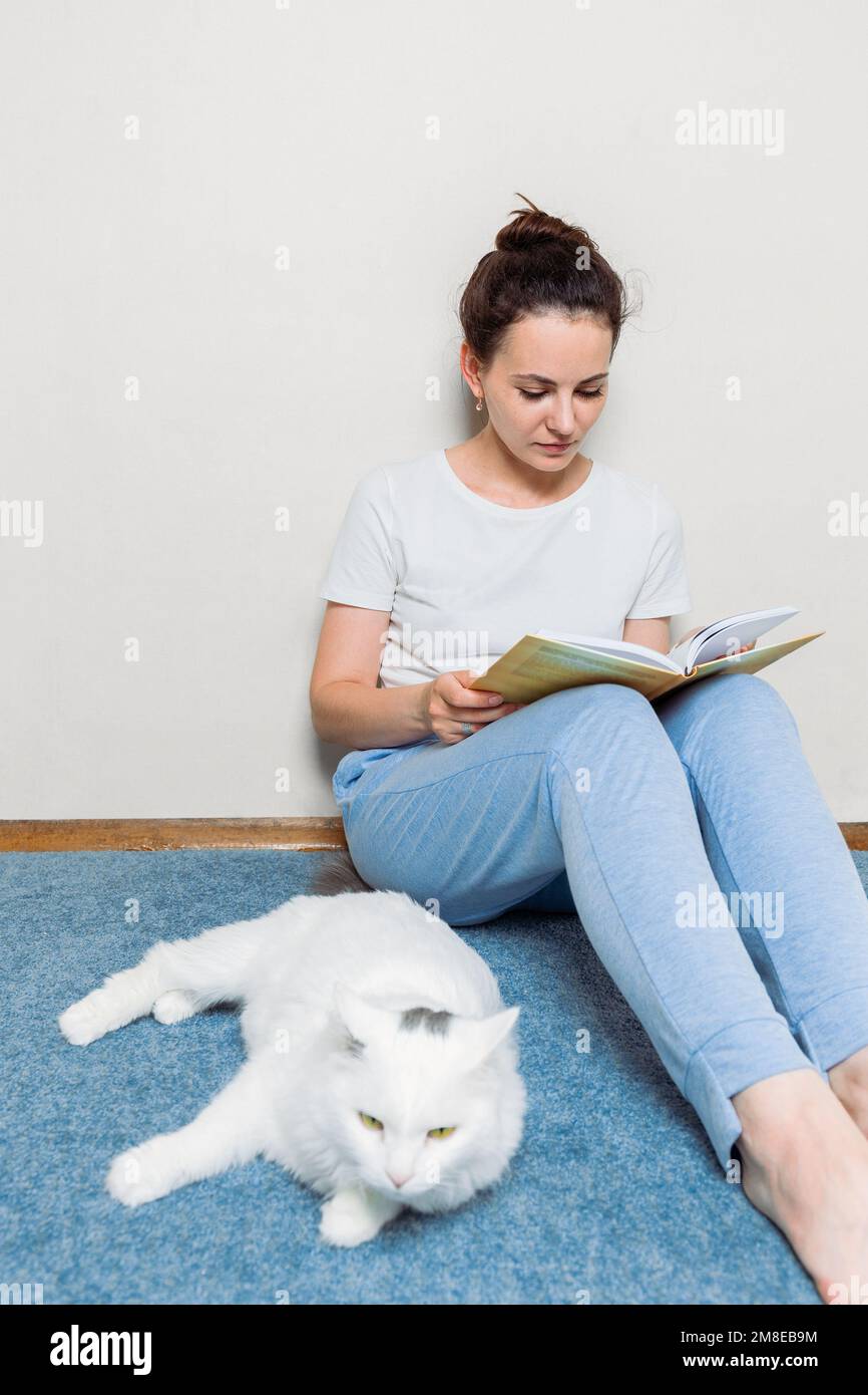 Girl reading book at cozy home. Girl smiling and petting furry cat ...