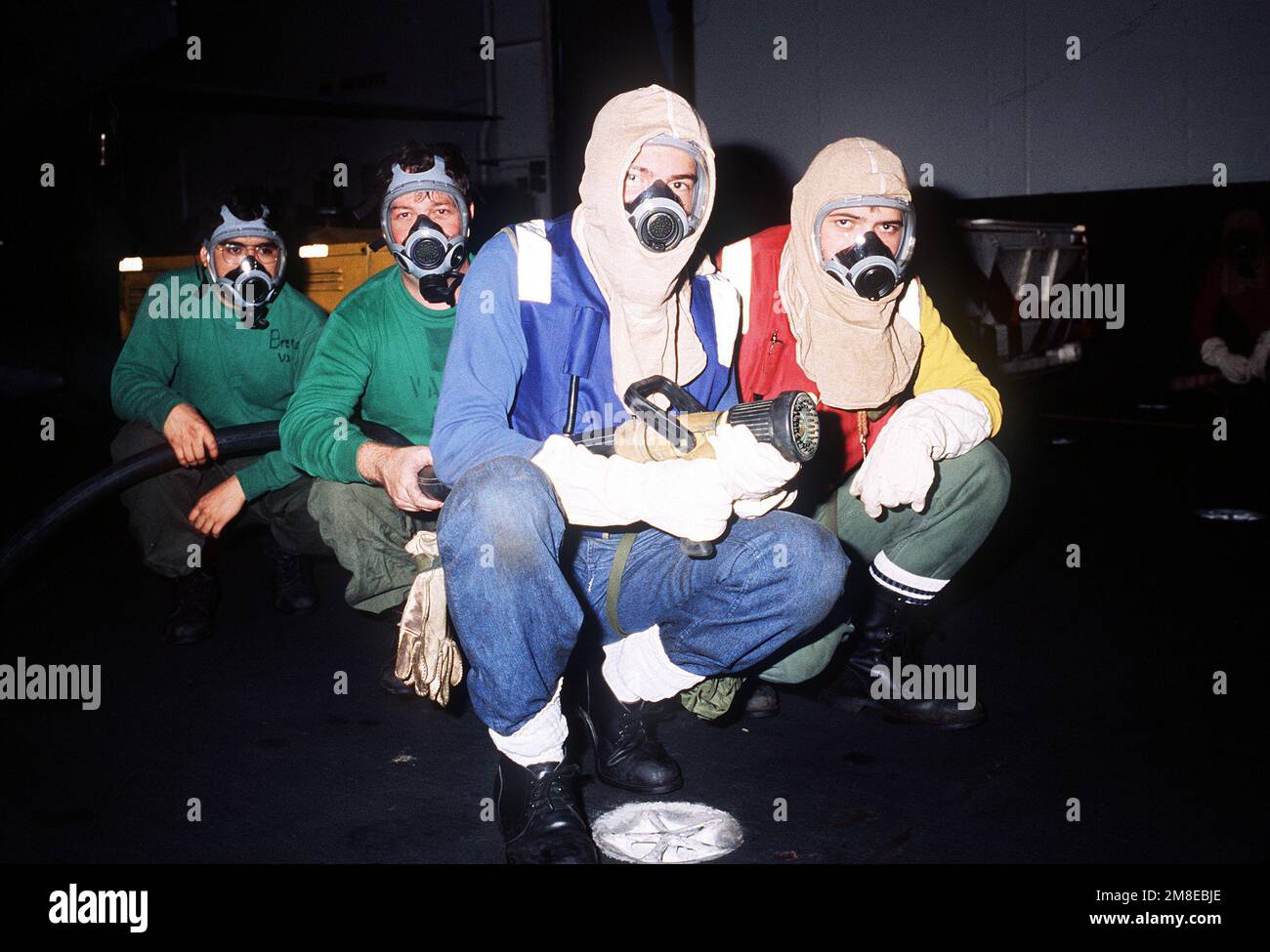 Flight deck crew members wearing MCU-2P gas masks man a fire hose ...