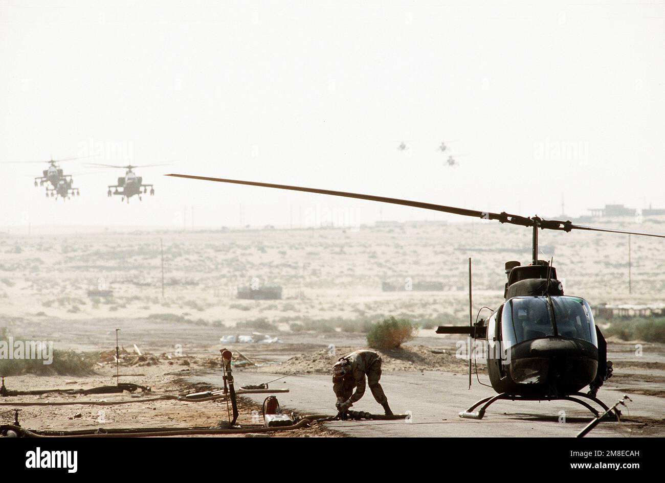 A soldier prepares to refuel an OH-58 Kiowa helicopter as several AH-64 ...