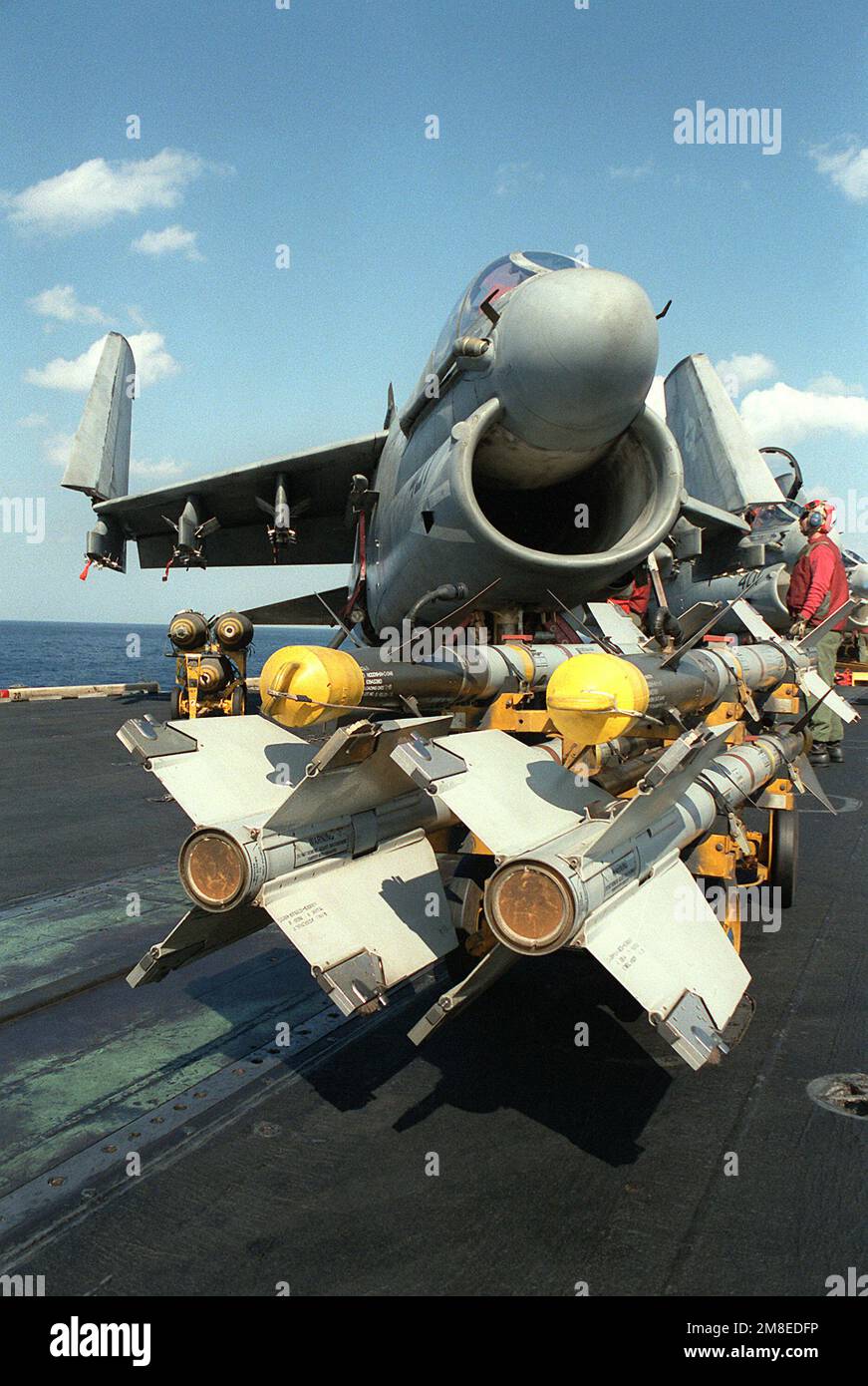 An ordnanceman prepares to load AIM-9 Sidewinder missiles, foreground ...