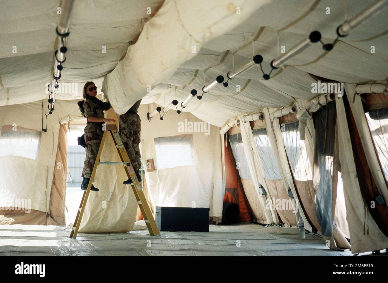Two airmen tie a fabric duct to the ceiling of a tent during Operation ...