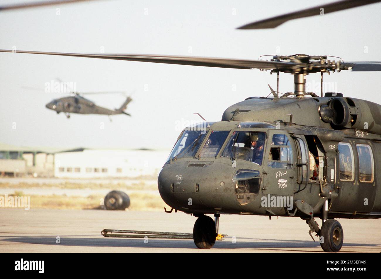 A UH-60A Black helicopter prepares for takeoff as another Black Hawk ...