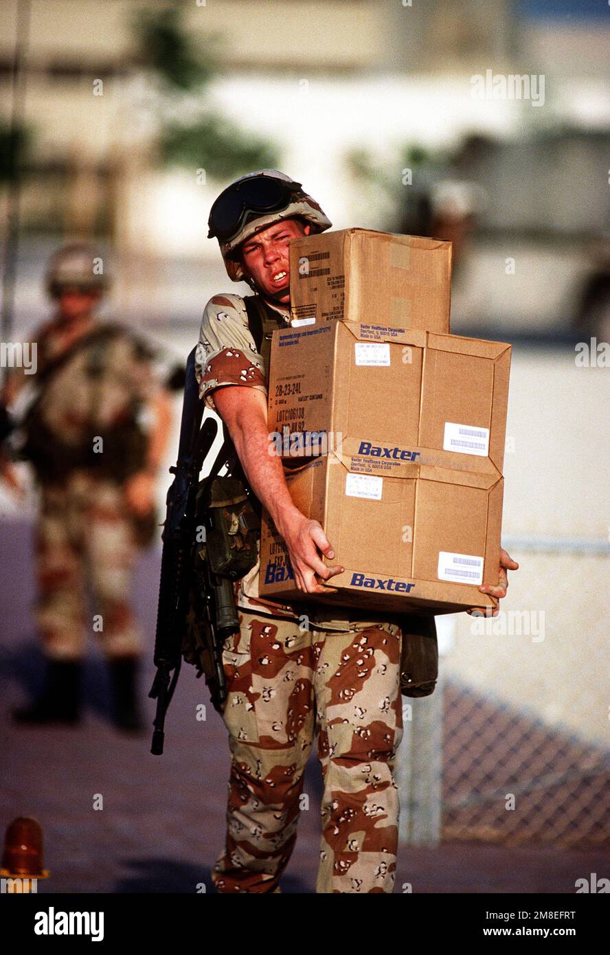 A soldier armed with an M-16A2 rifle carries boxes of medical supplies ...
