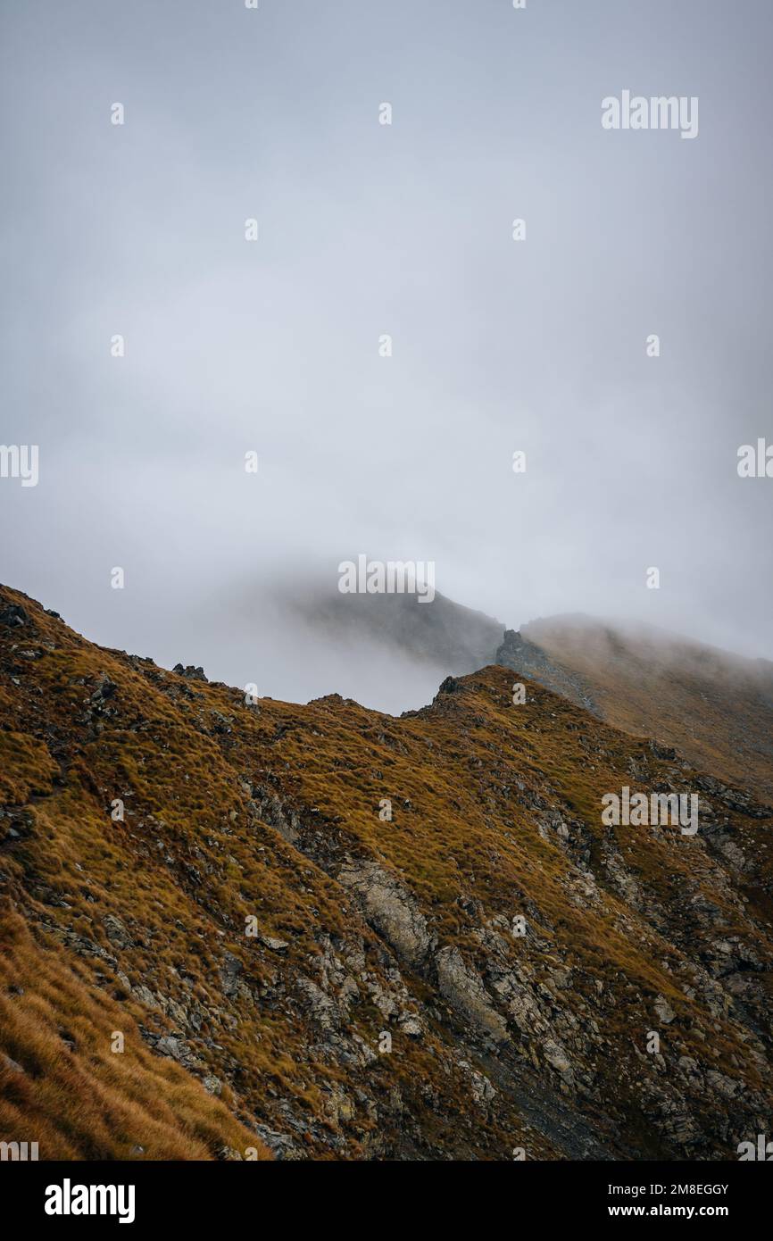 A vertical shot of a mountain range covered with clouds on a foggy day ...