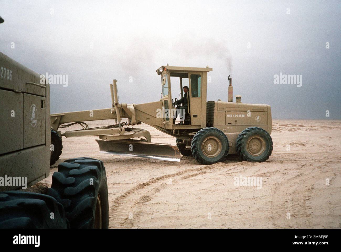 A Seabee drives a John Deere 670 motor grader through a camp being ...