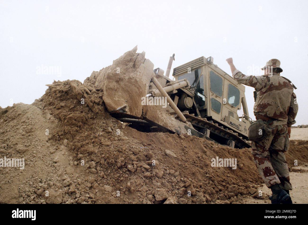 A Seabee signals to the driver of a bulldozer as members of Naval ...