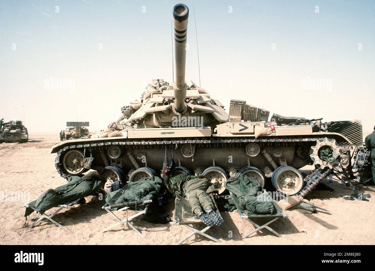 Two Marine tank crewmen stretch out on cots beside their M-60A1 tank at ...