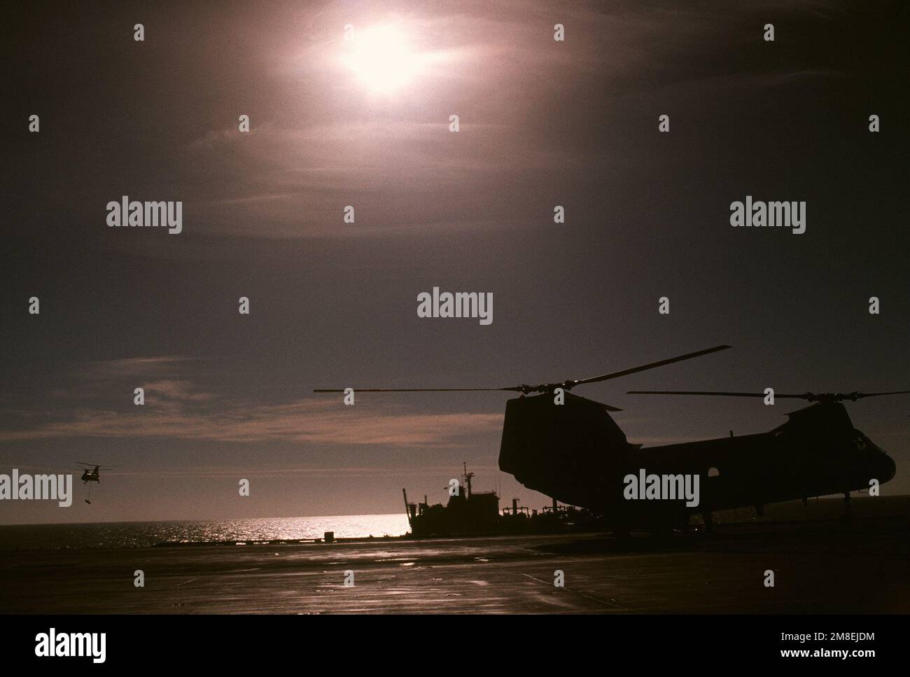A UH-46 Sea Knight helicopter is silhouetted by the sun as it sits on ...