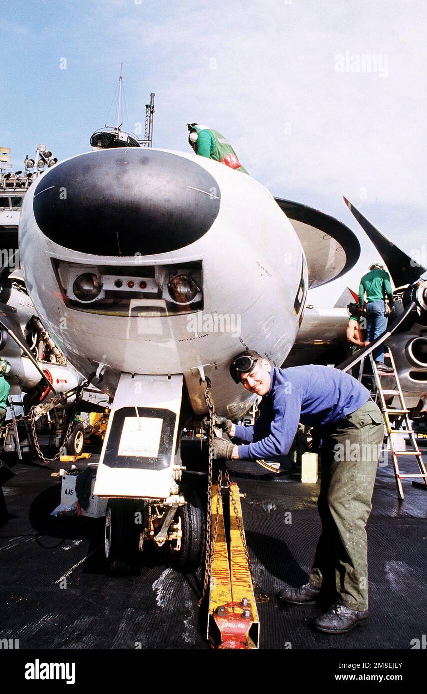 A flight deck crew member connects tie-down chains to an E-2C Hawkeye ...