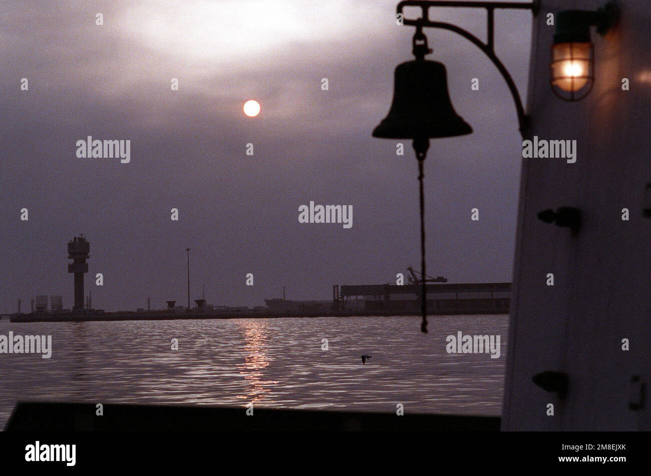A ship's bell is silhouetted against the smoke-filled sky following ...