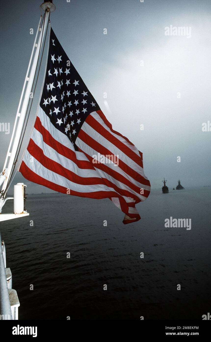 The national ensign flies from the stern of a U.S. Navy ship at anchor ...